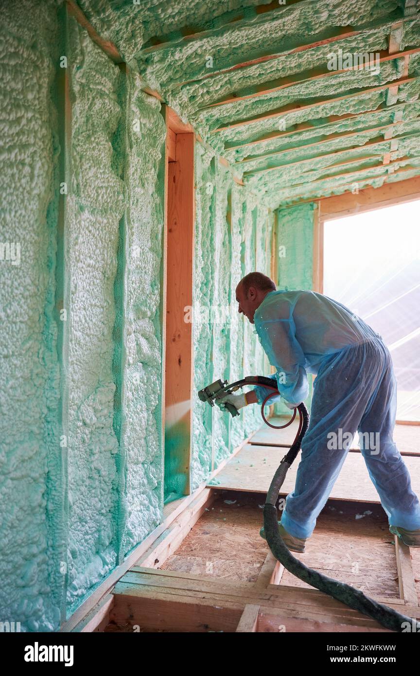 Male builder insulating wooden frame house. Man worker spraying ...