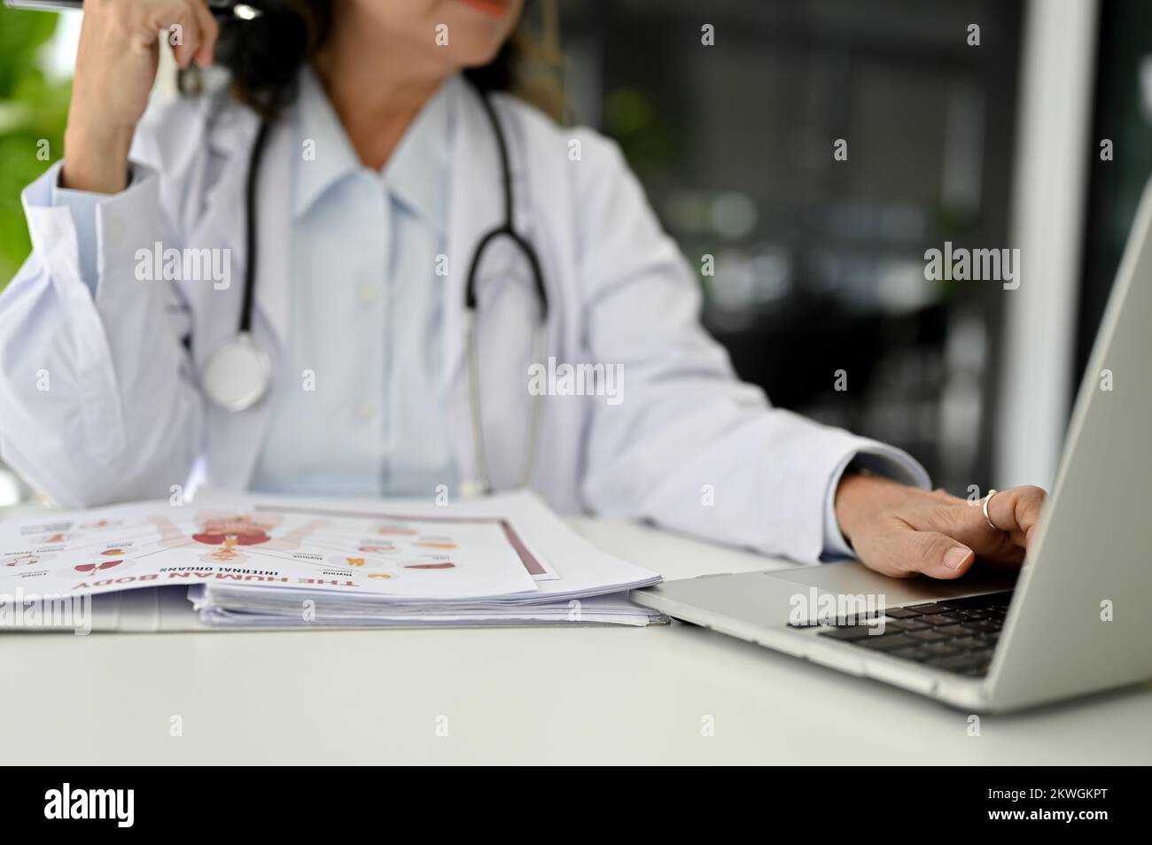Professional Asian aged female doctor in white gown using laptop ...
