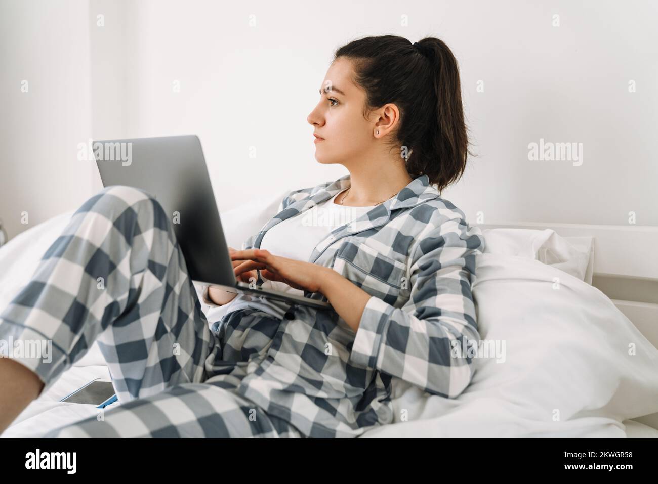 Young woman wearing pajama using laptop while resting on bed at home ...