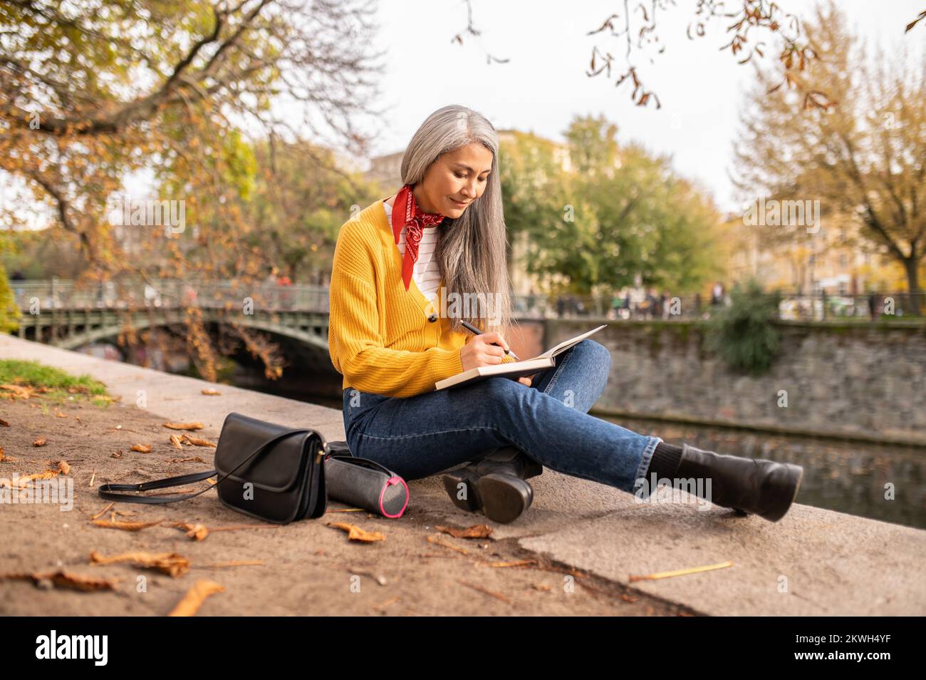 Woman sitting on the river bank, making notes and looking inspired ...
