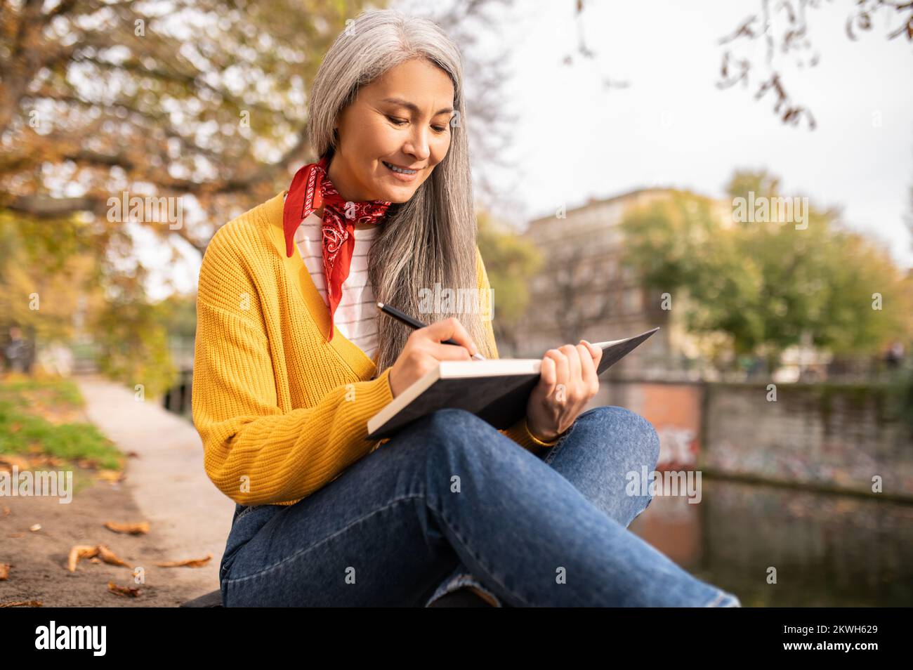 Woman sitting on the river bank, making notes and looking inspired ...