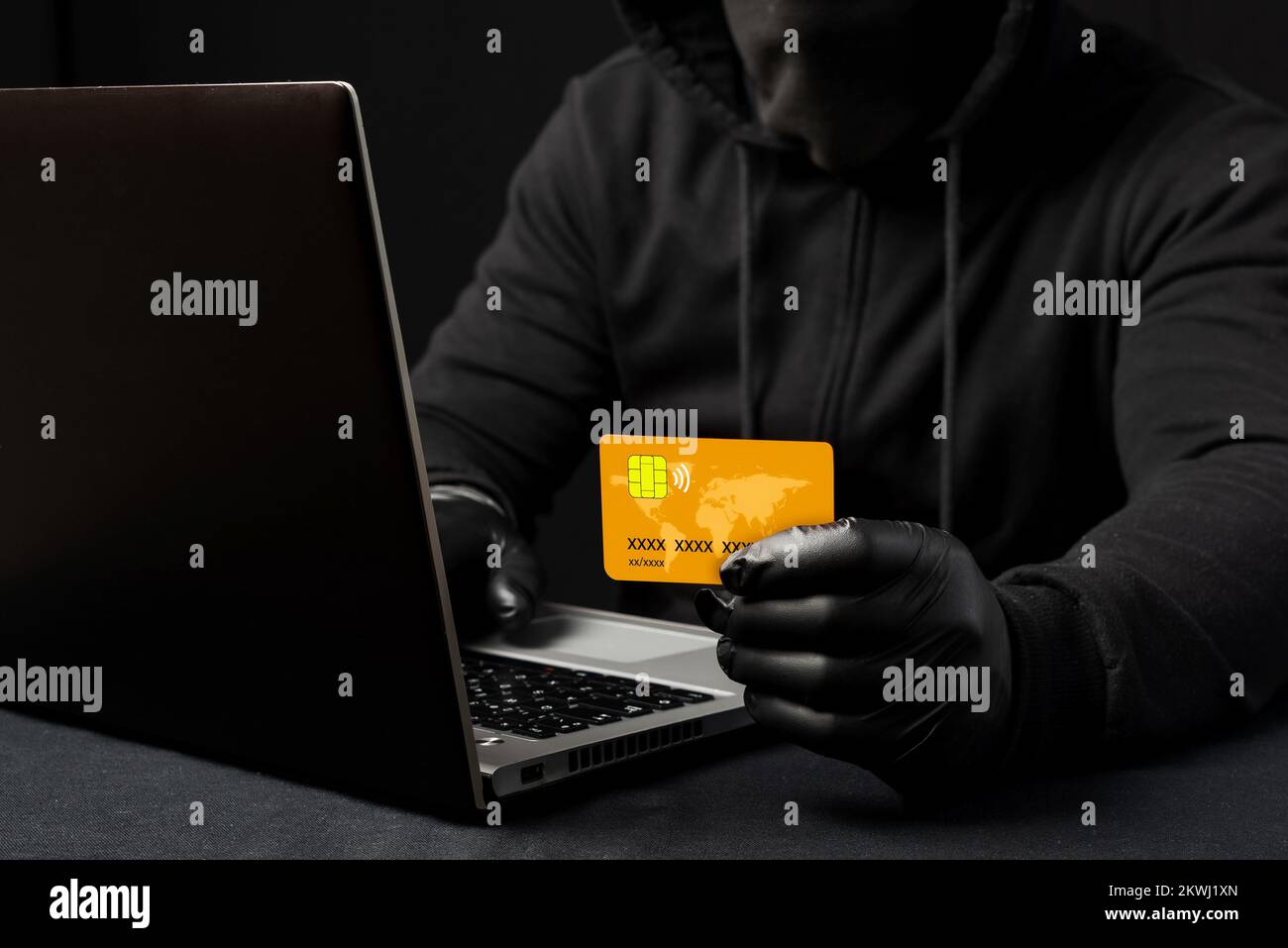 A hooded cybercriminal, holding a credit or debit card. Internet scams ...