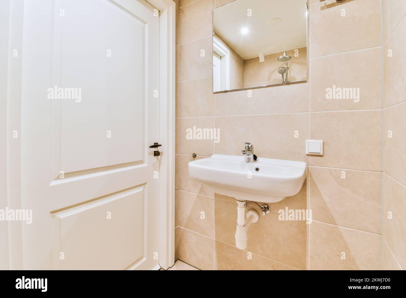 Cupboard with sink and mirror attached to tiled wall near door and ...