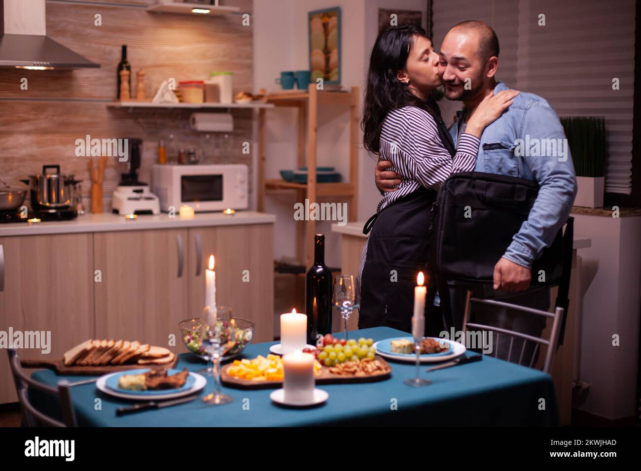 Kissing husband cheek while greeting him in kitchen for romantic dinner ...