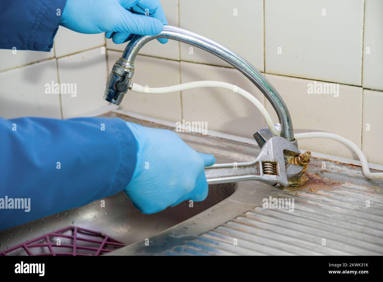 The plumber unscrews the old rusty faucet in the kitchen wrench. The ...