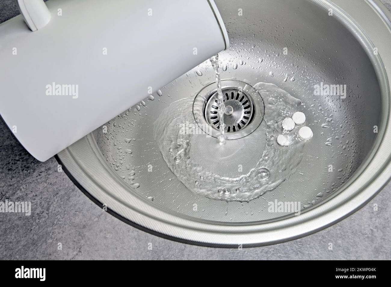 Hot water is poured from a white electric kettle into a metal kitchen sink with disinfectant ...