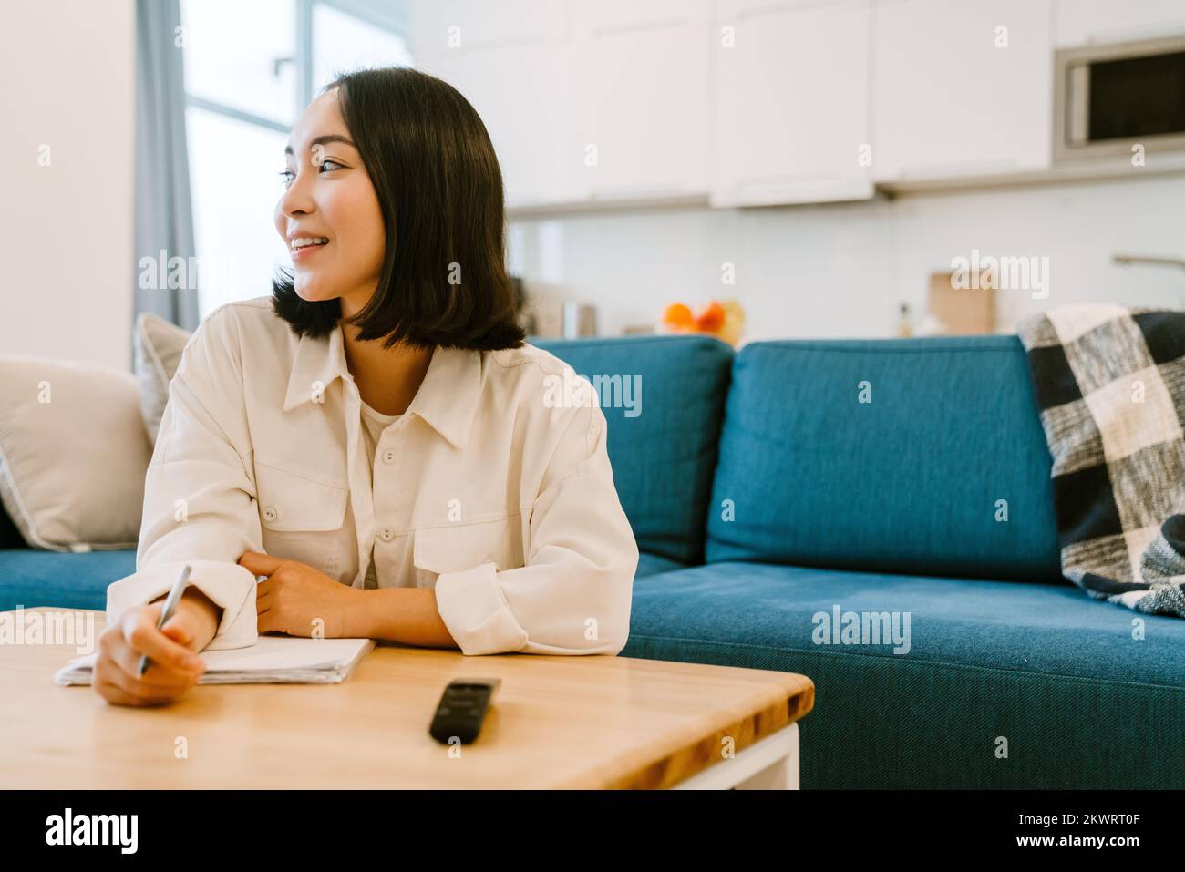 Young cute smiling asian woman writing notes in cozy spacious living ...