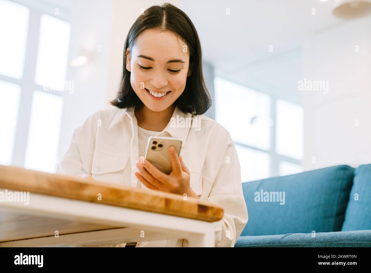 Young cute smiling asian woman holding phone and looking on the screen ...