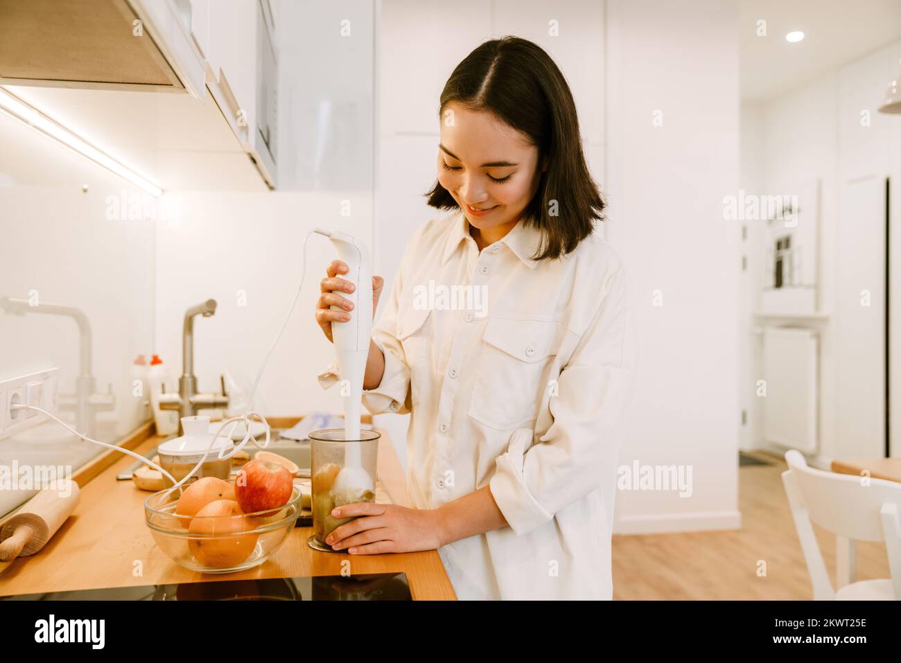 Young cute beautiful smiling asian girl cooking smoothie in cozy ...