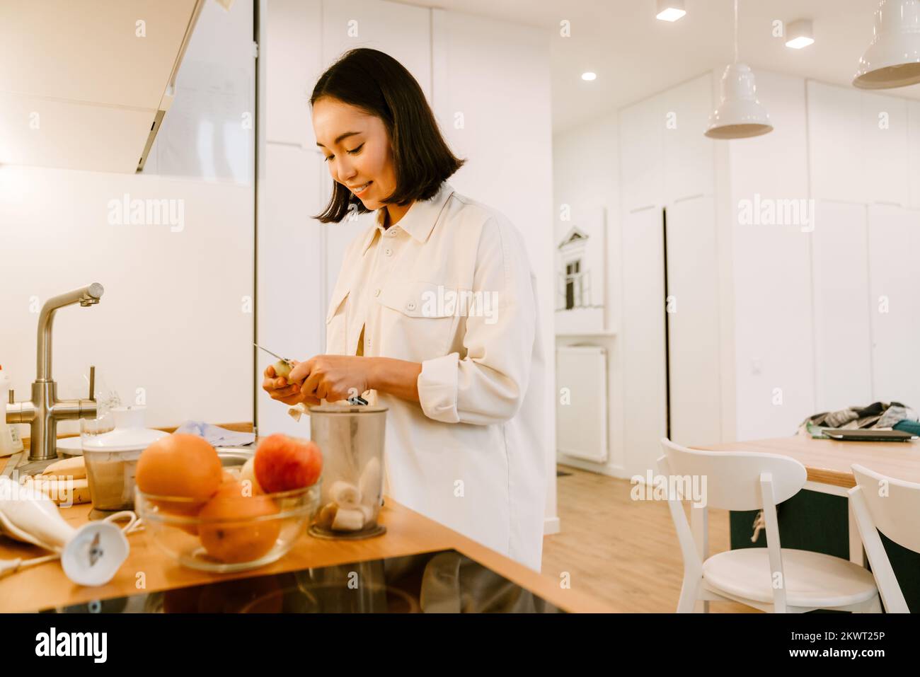 Young cute beautiful smiling asian girl cooking smoothie in cozy ...