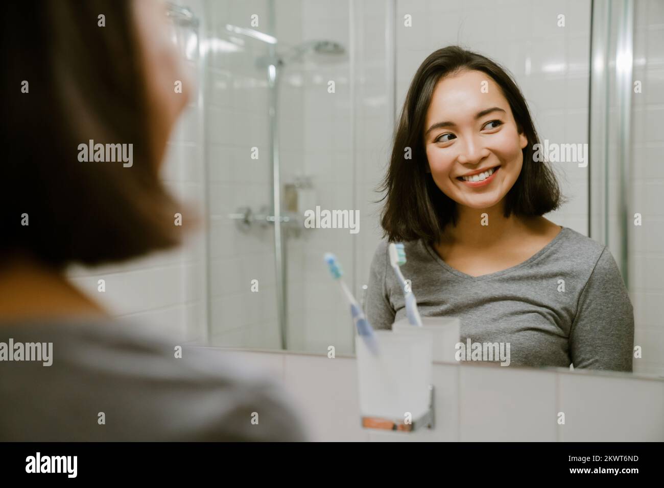 Young smiling asian girl standing in front of a mirror and looking ...
