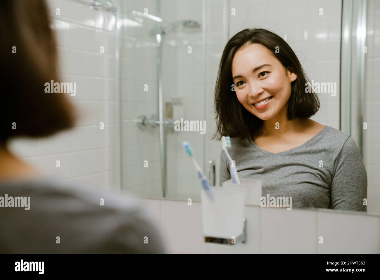Young Smiling Asian Girl Standing In Front Of A Mirror In The Bathroom