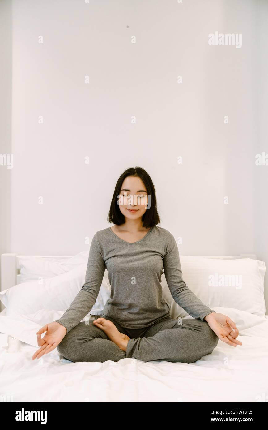 Young calm asian girl in home suit meditating on the bed at home Stock ...