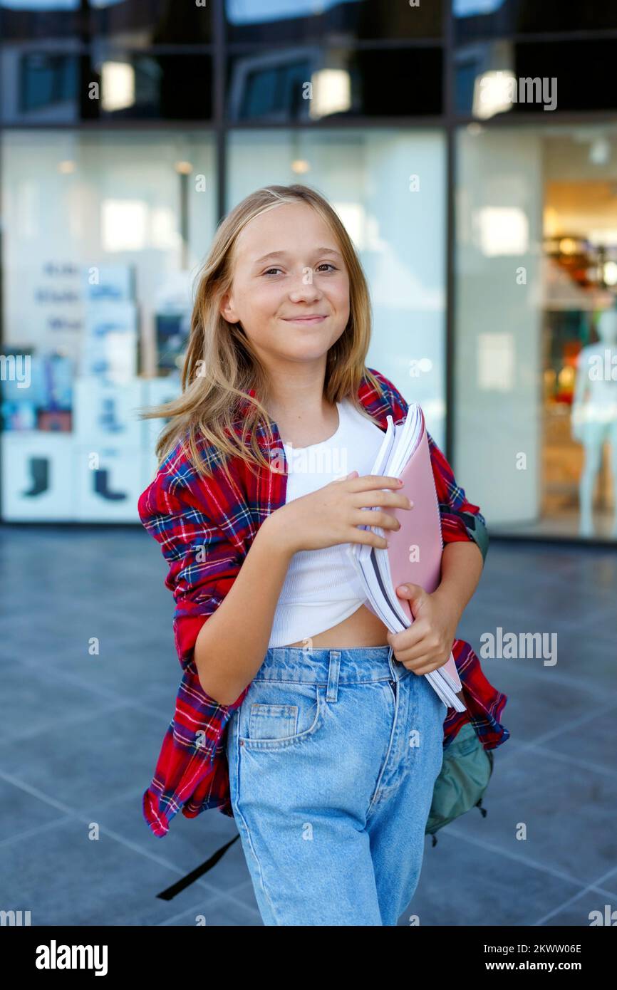 Smiling girl standing on street and holding notebooks. Child outdoor ...
