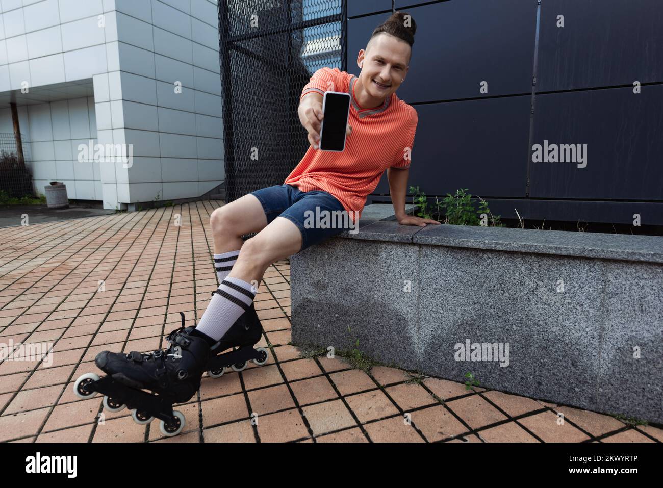 Smiling man in rollers holding smartphone with blank screen on urban ...