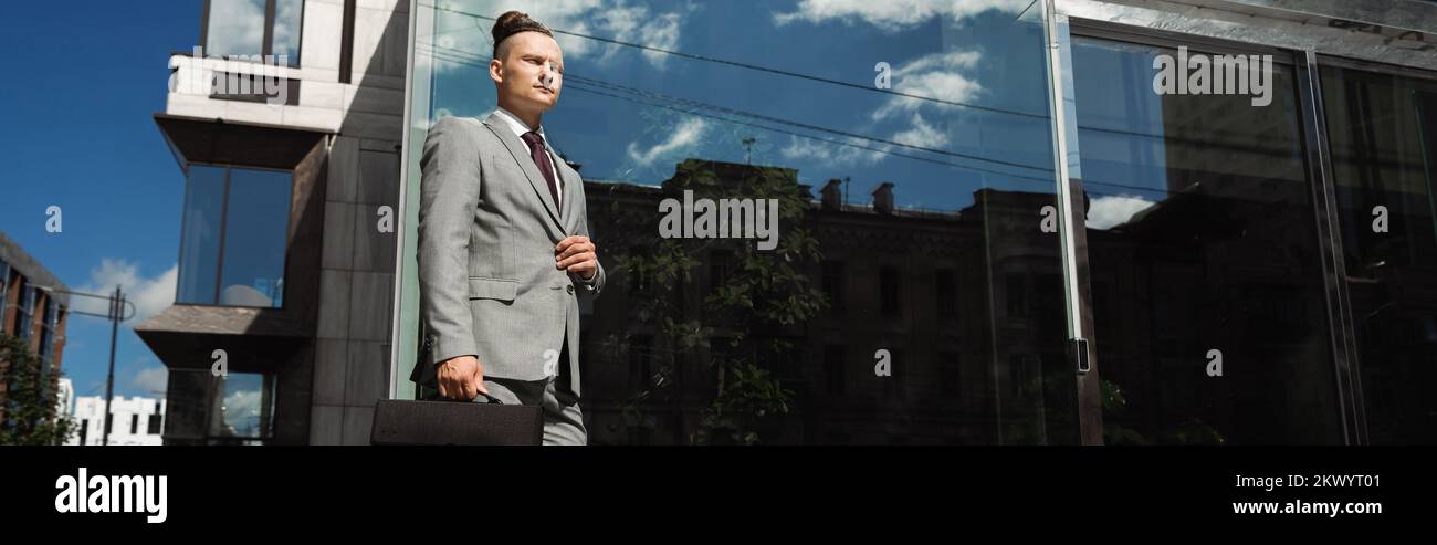 young and trendy businessman in grey suit looking away on street near ...