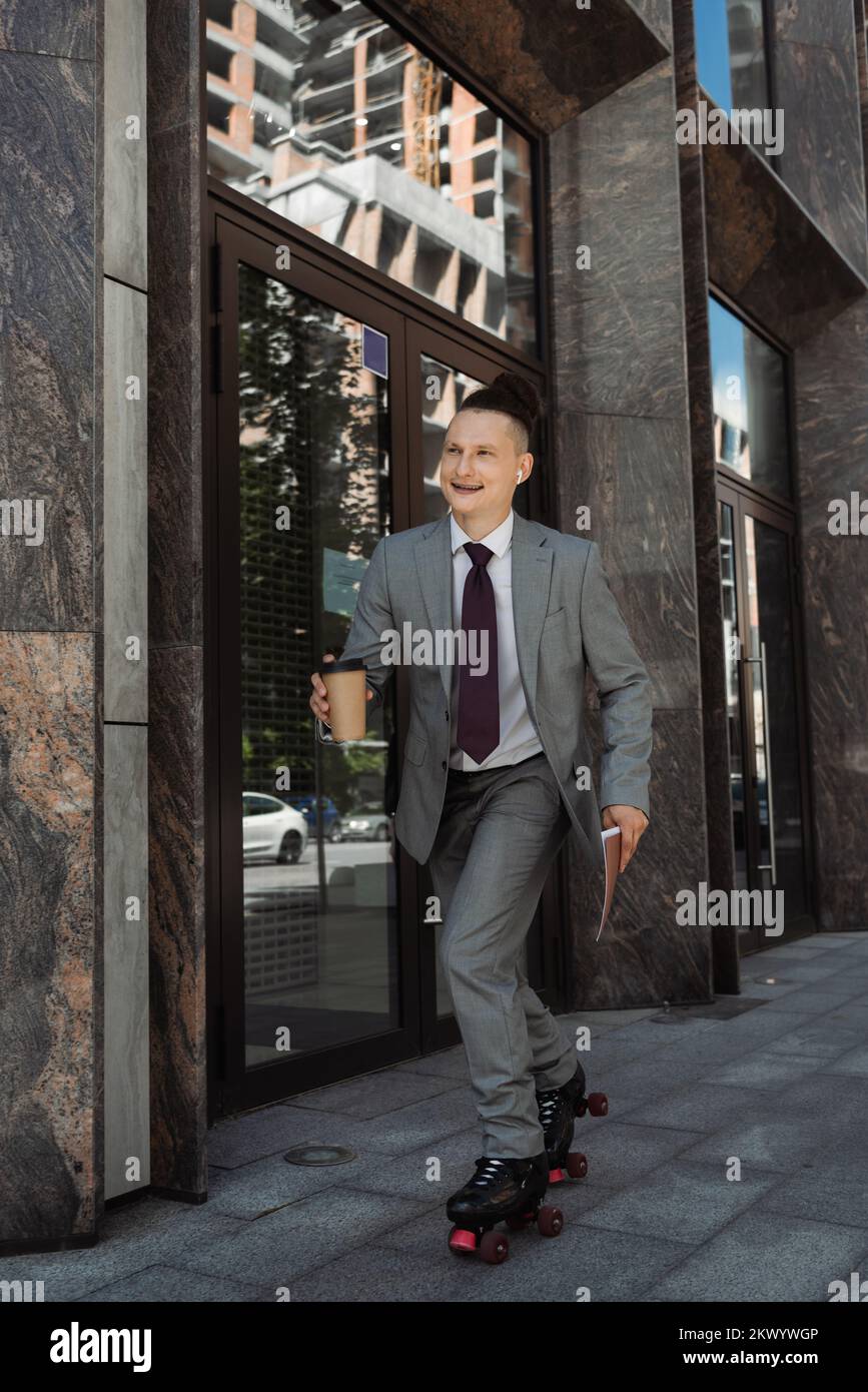 happy man in business suit roller skating with paper cup and folder on ...