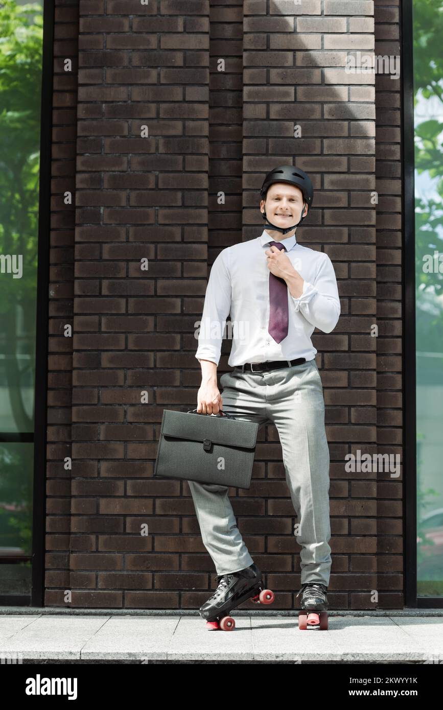cheerful roller skater in formal wear fixing tie and smiling at camera ...