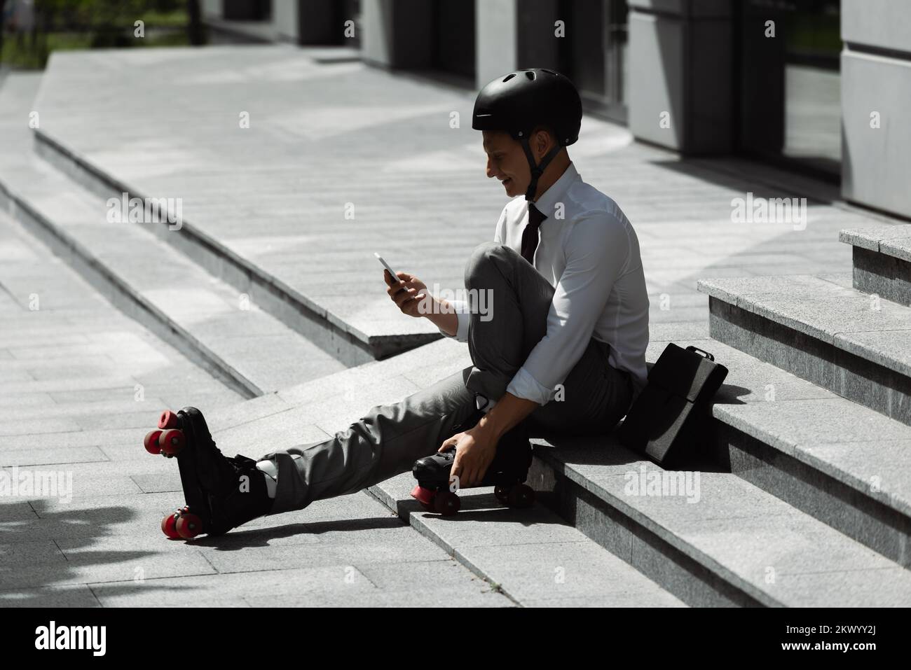 smiling roller skater in formal wear and helmet messaging on smartphone ...