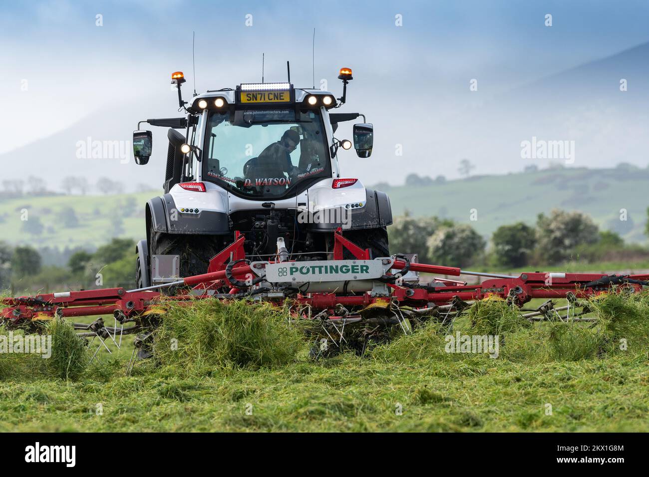 Contractor driving a Valtra tractor and spreading grass in a silage ...