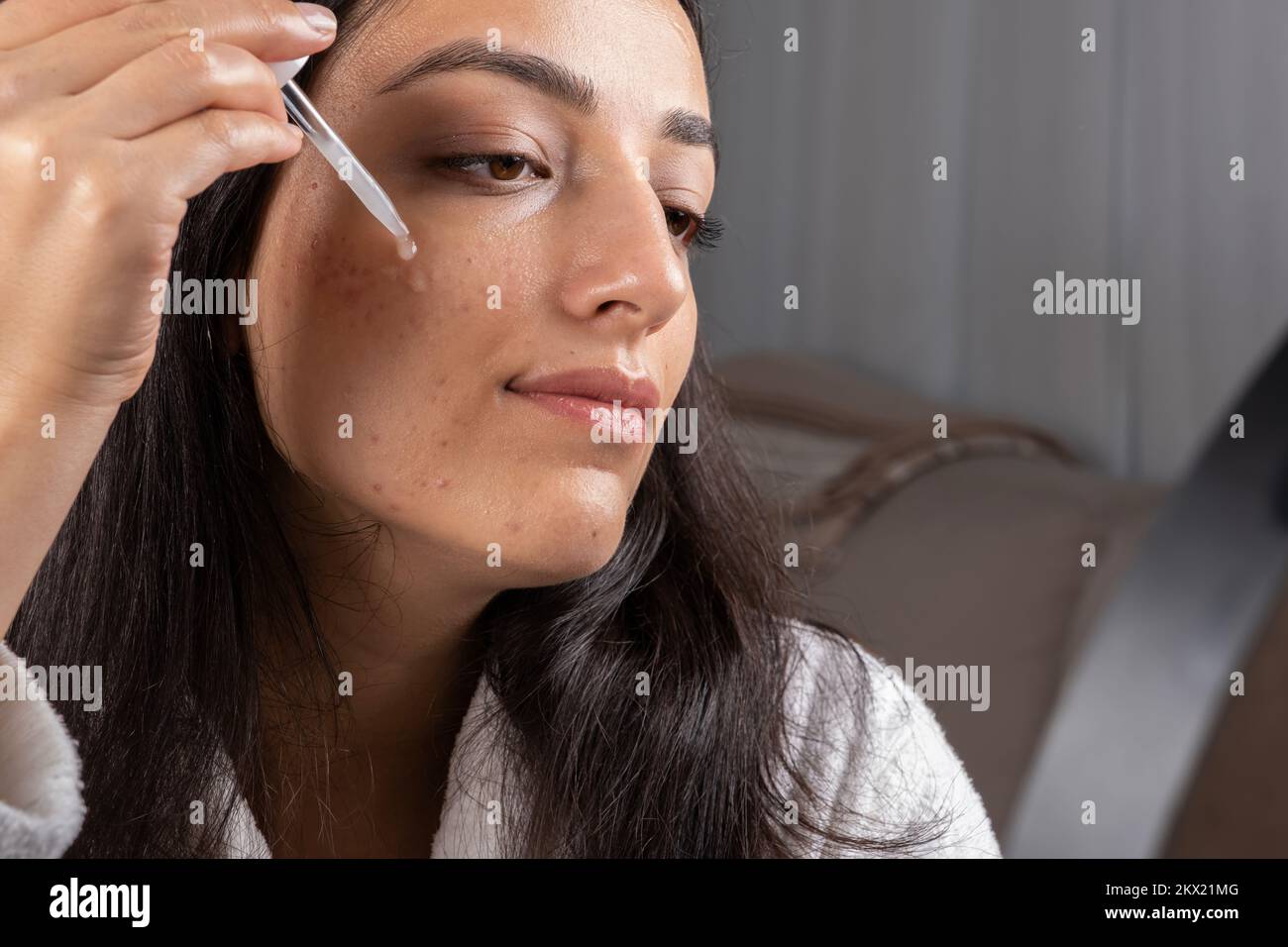 Woman dripping skin care serum from dropper on her cheek. Caucasian ...