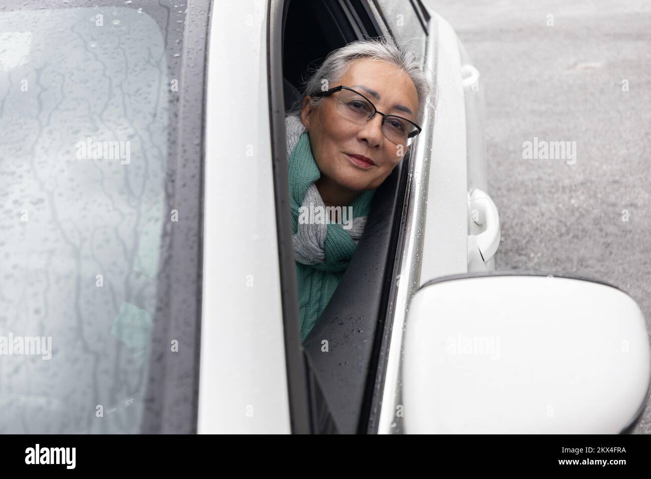 A gray-haired lady looks out of a car window and smiles at the camera ...