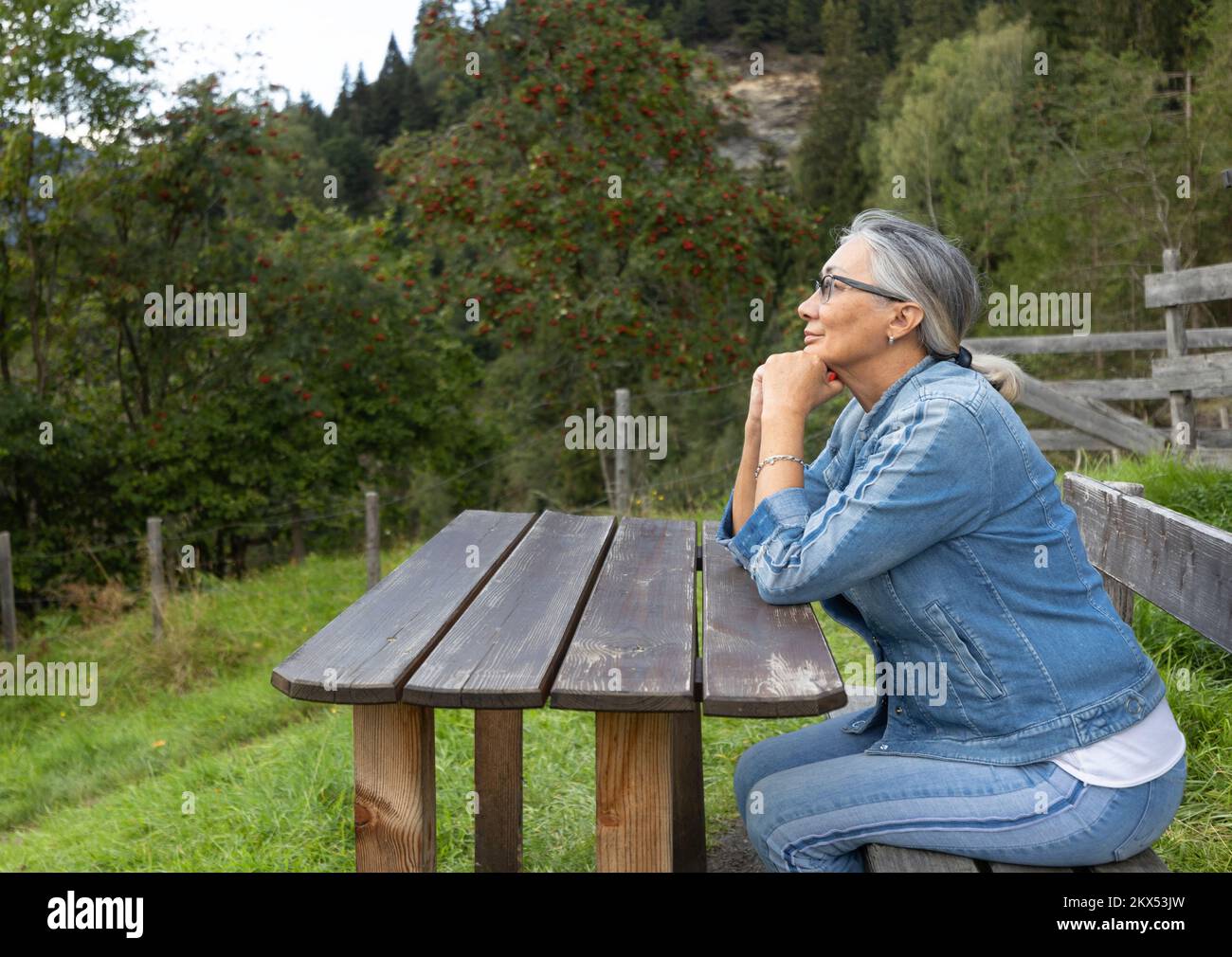 A gray-haired woman sits at a wooden table in the countryside at the ...