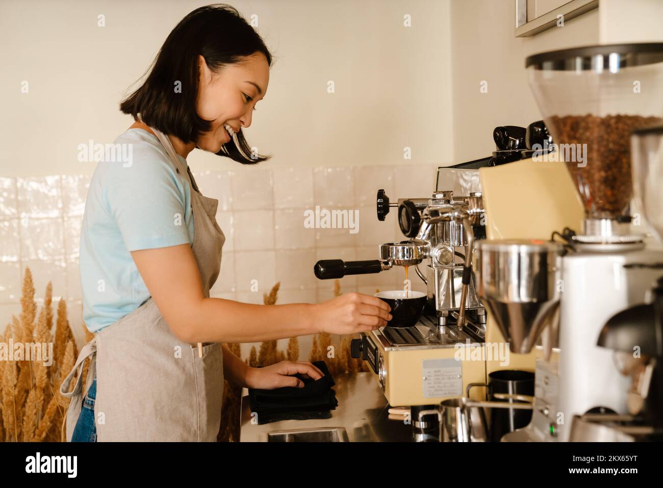 Young asian barista woman wearing apron smiling while making coffee in ...