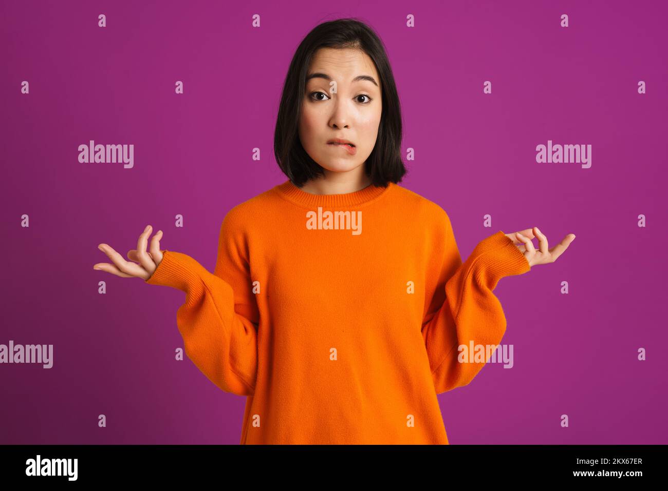 Perplexed asian woman frowning while gesturing isolated over purple ...