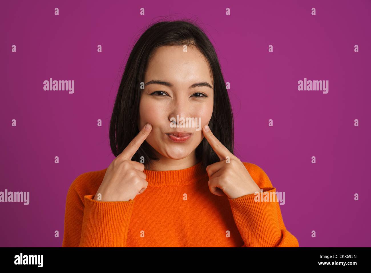 Young asian woman making kiss lips while pointing her cheeks isolated ...