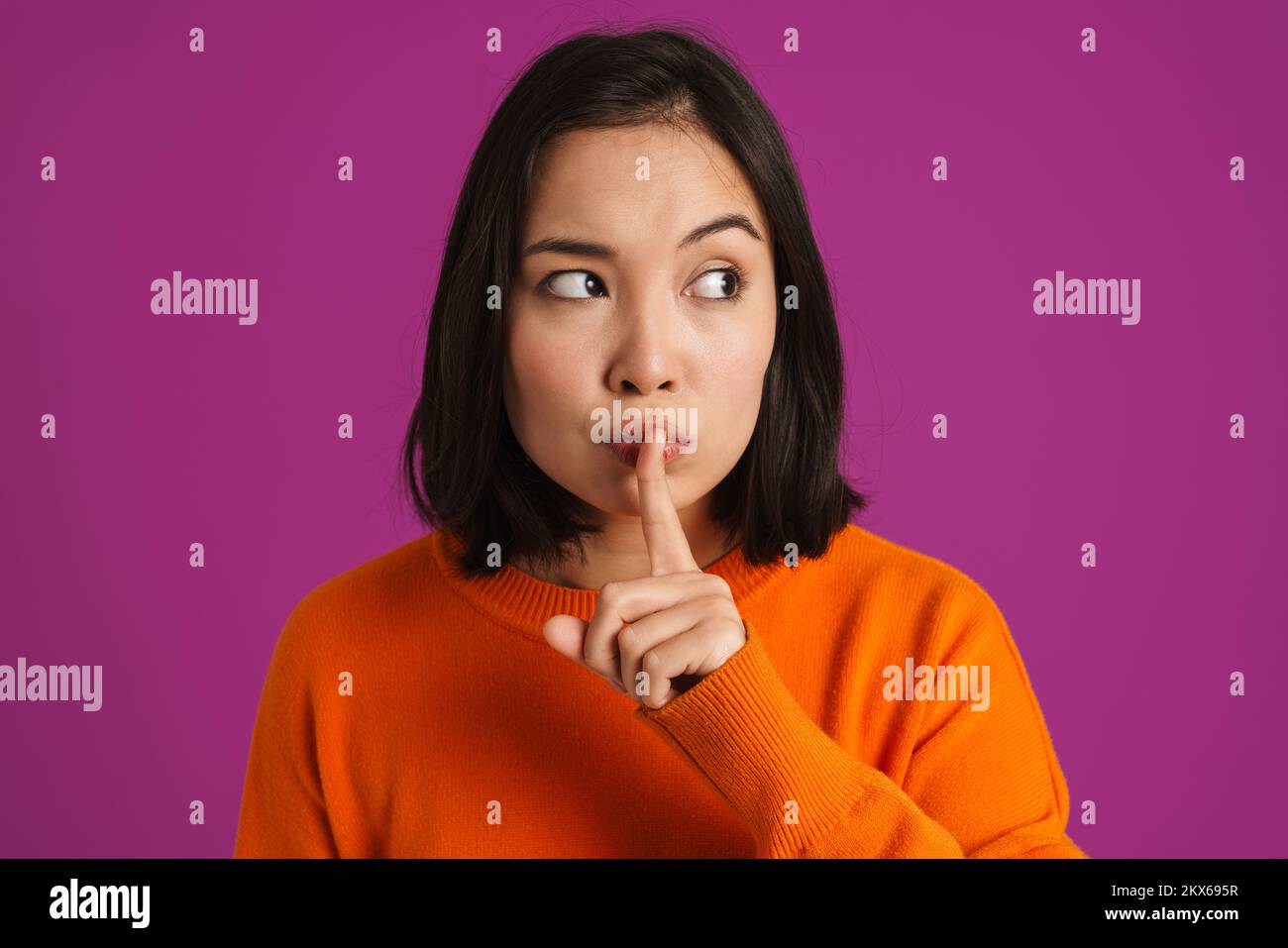 Young asian woman frowning while making silence gesture isolated over ...