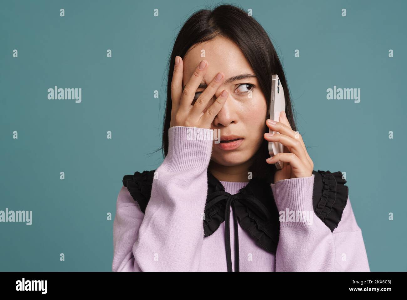 Young asian woman covering her face and talking on mobile phone ...