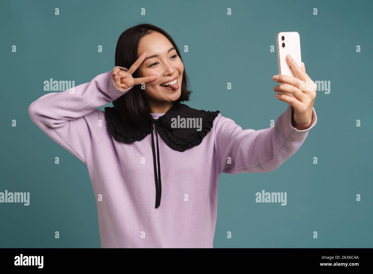 Young asian woman gesturing while taking selfie on cellphone isolated ...