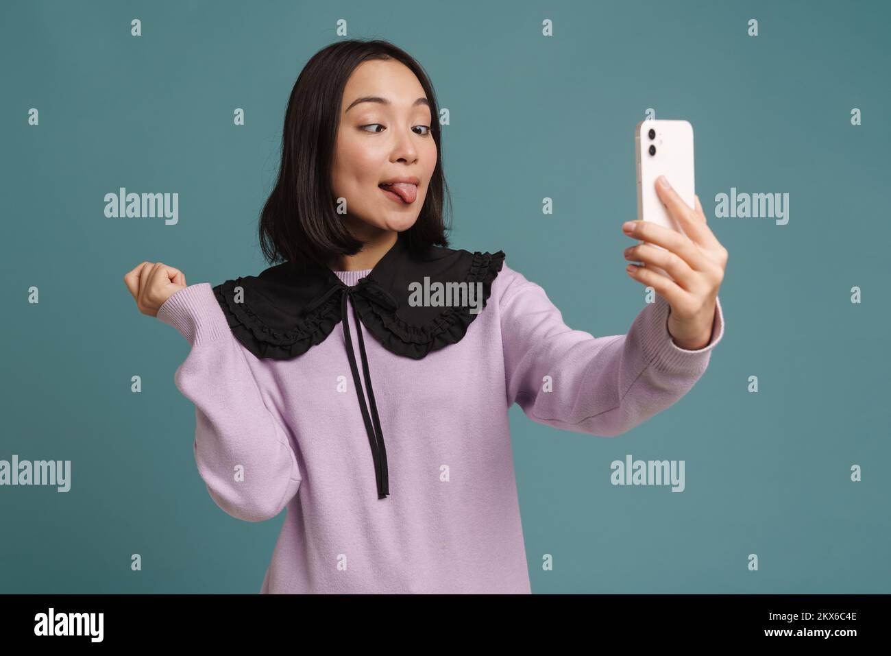 Young asian woman showing her tongue while taking selfie on cellphone ...