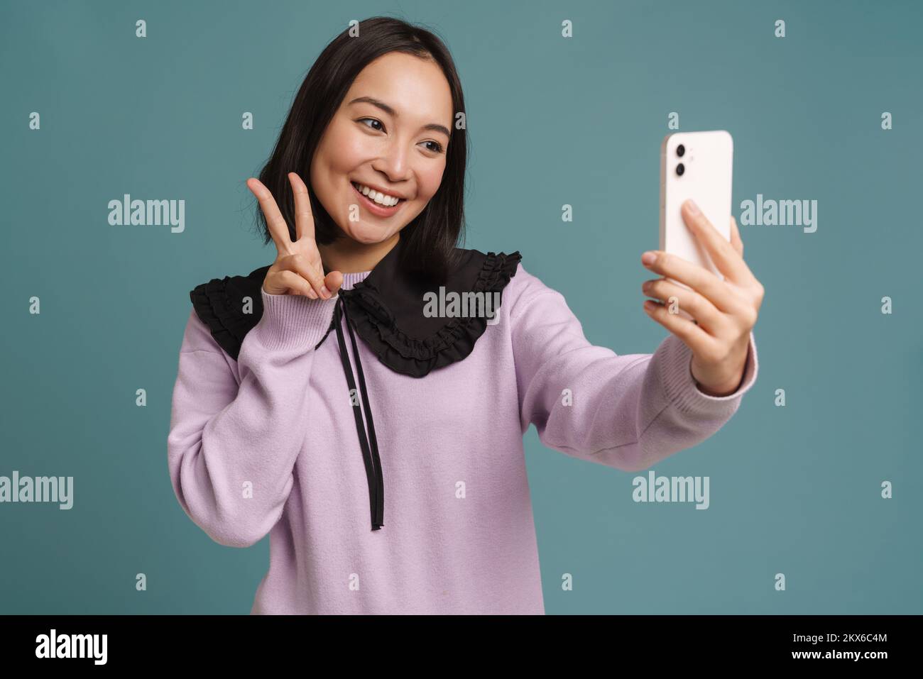 Young asian woman gesturing while taking selfie on cellphone isolated ...