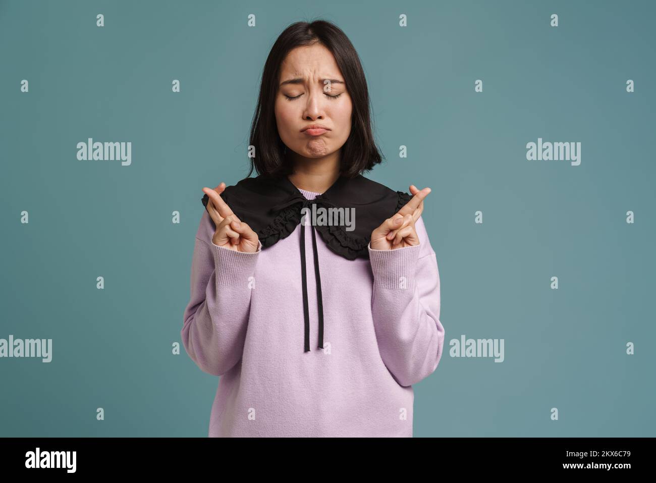 Young asian woman frowning while fingers crossed for good luck isolated ...