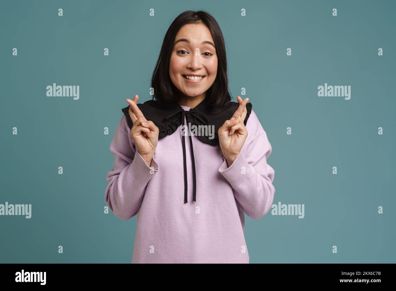 Young asian woman laughing while fingers crossed for good luck isolated ...
