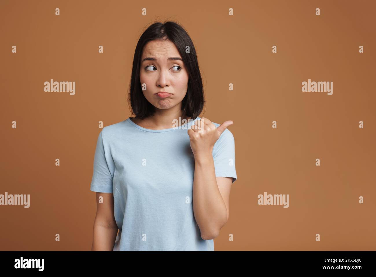 Perplexed asian woman wearing t-shirt pointing finger aside isolated ...