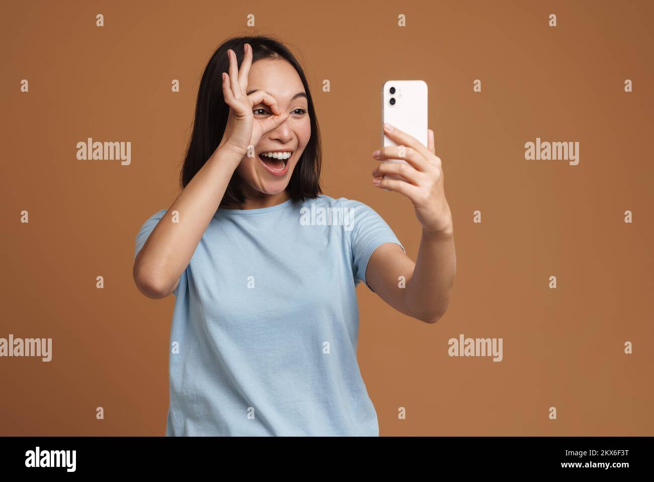 Young asian woman gesturing while taking selfie on cellphone isolated ...