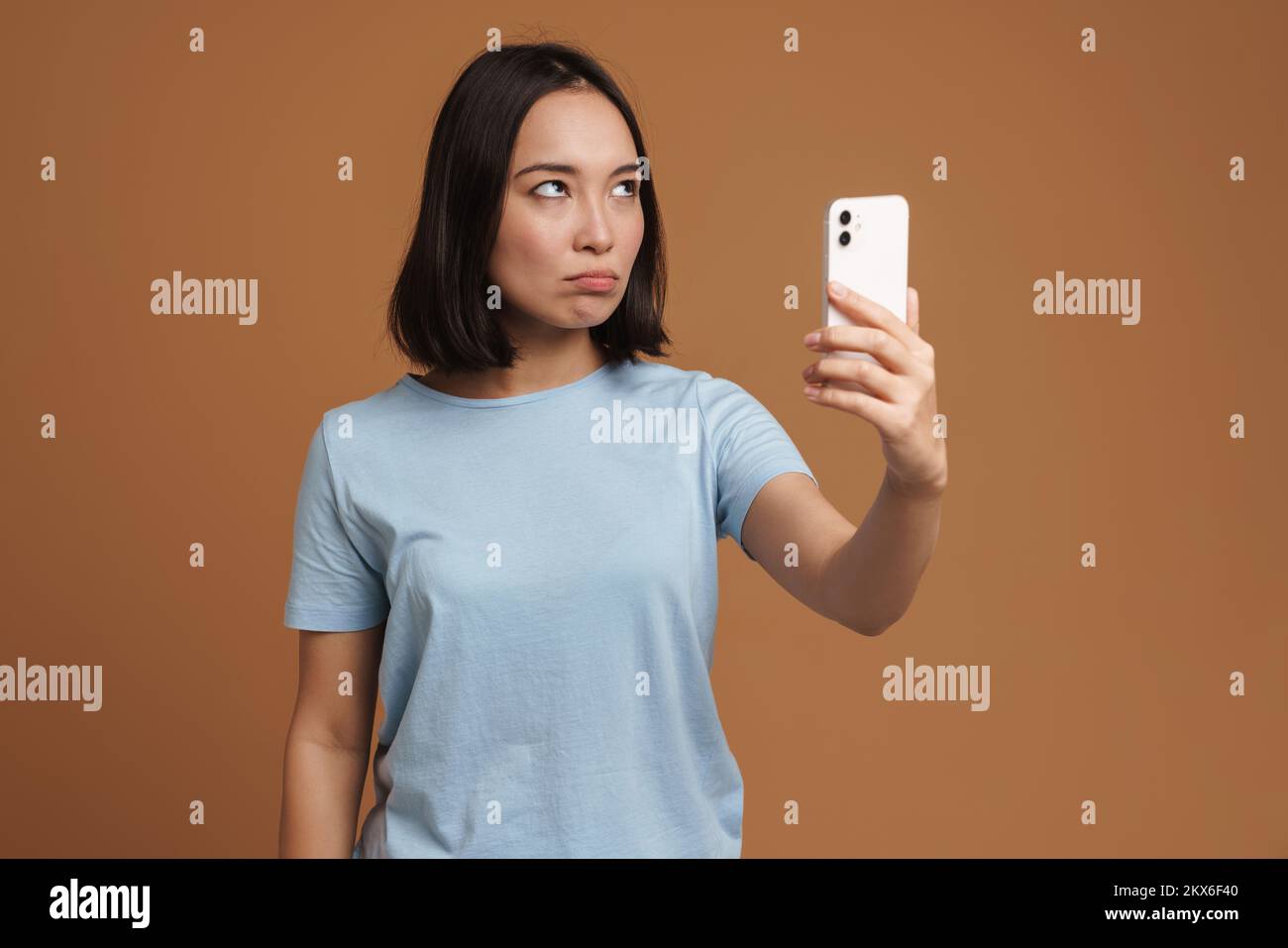 Displeased asian woman taking selfie photo on cellphone isolated over ...