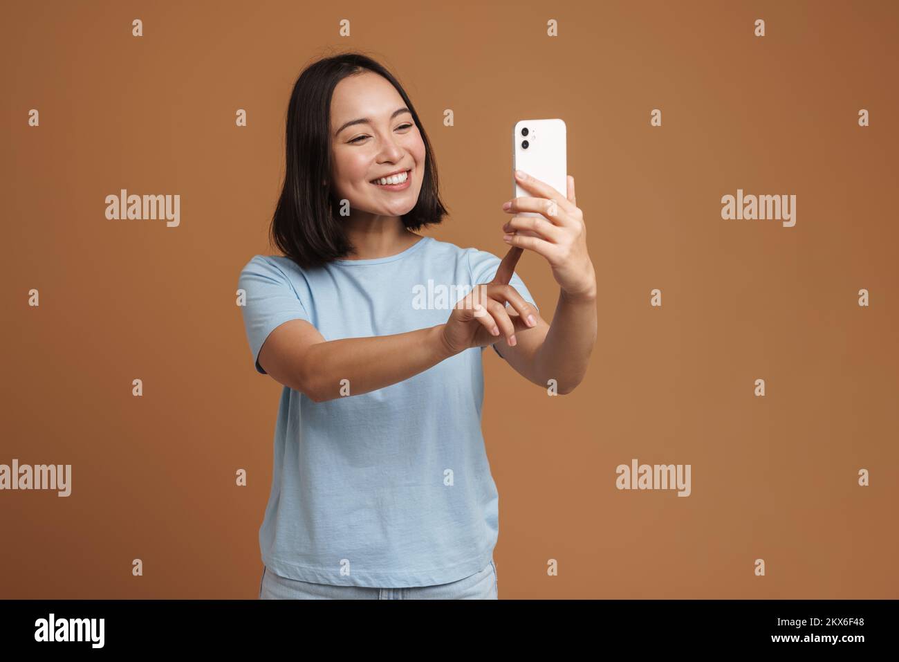 Young asian woman smiling while taking selfie on cellphone isolated ...
