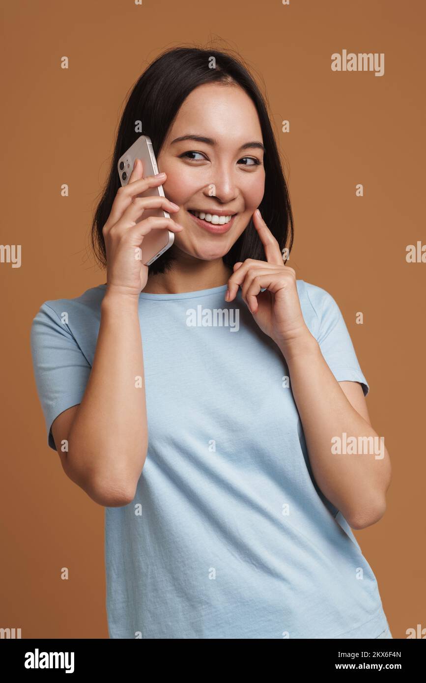 Young asian woman wearing t-shirt laughing while talking on cellphone ...