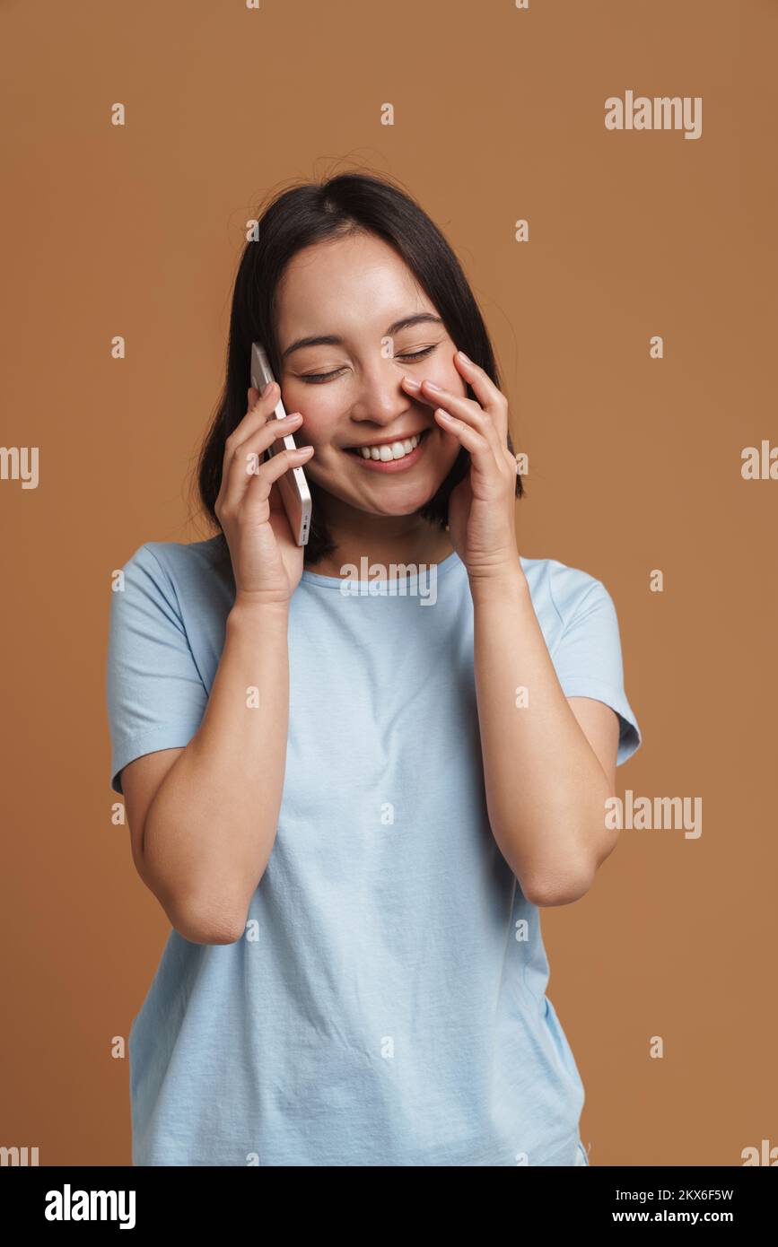 Young asian woman wearing t-shirt laughing while talking on cellphone ...