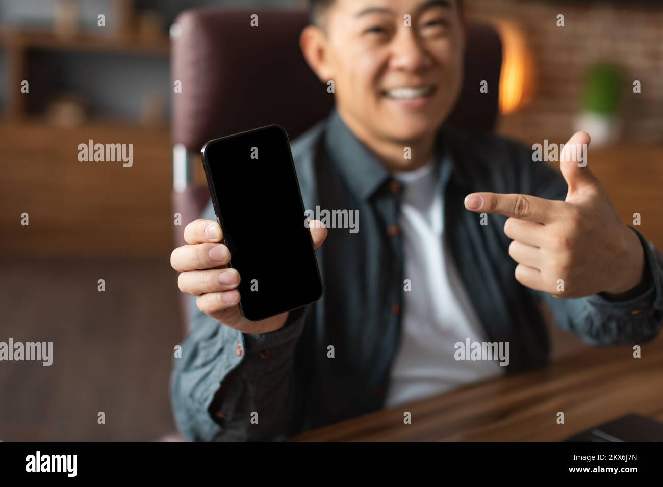 Glad adult asian man pointing finger at smartphone with empty screen at ...