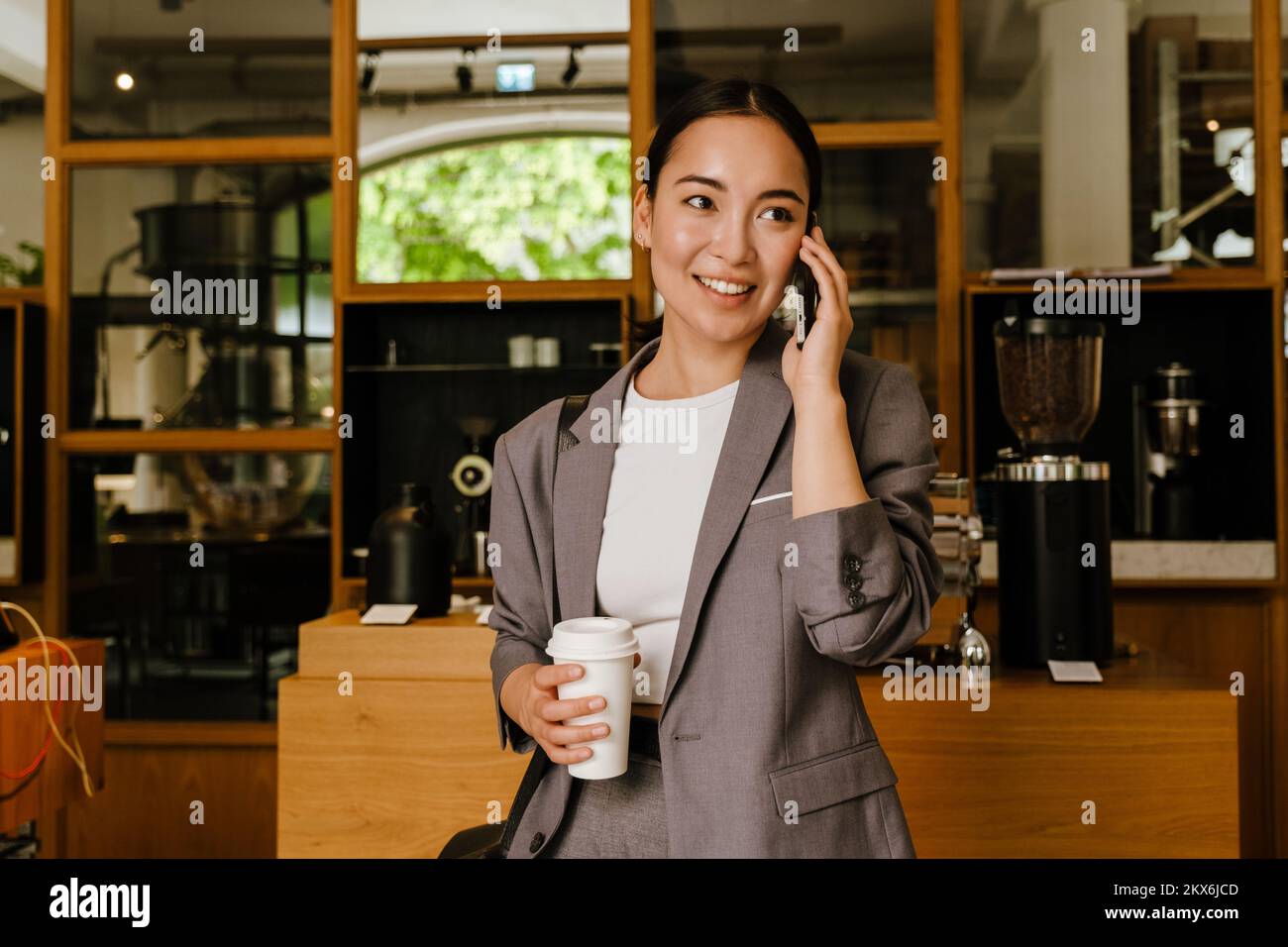 Asian young businesswoman drinking coffee and talking on cellphone ...