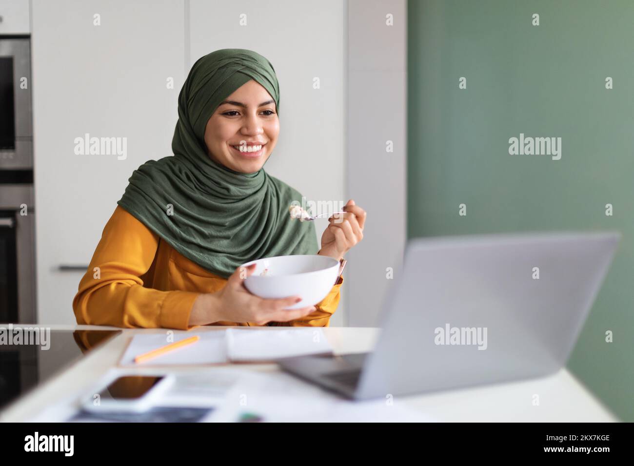 Young Muslim Woman Watching Videos On Laptop While Eating Breakfast In ...