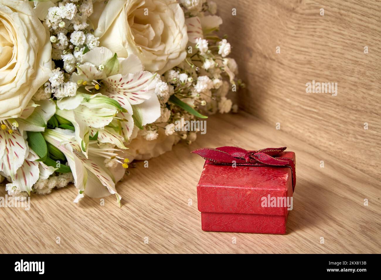 Red gift box with bow on lid, bouquet of white flowers on wooden ...