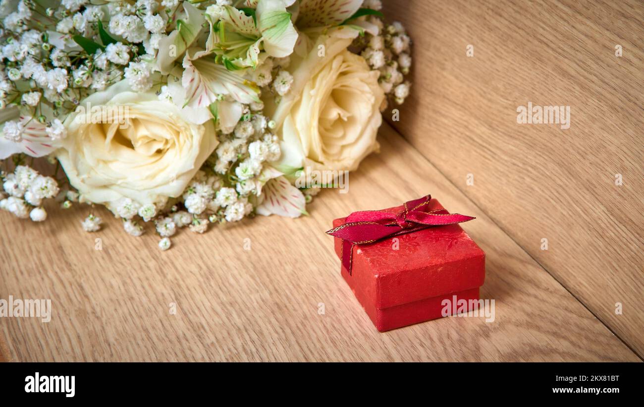 Red gift box with bow on lid, bouquet of white flowers on wooden ...
