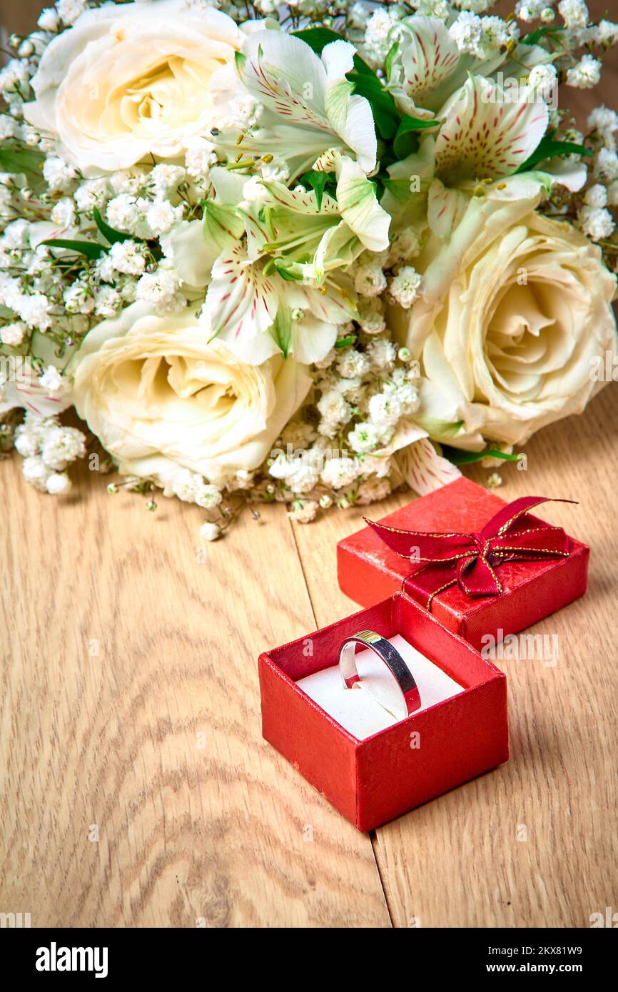 Silver ring in red gift box, bouquet of white flowers on wooden ...