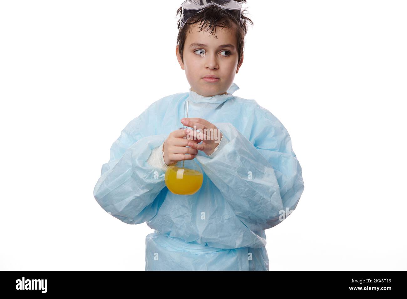 Smart teenage boy in lab coat holding a glass flask with yellow ...